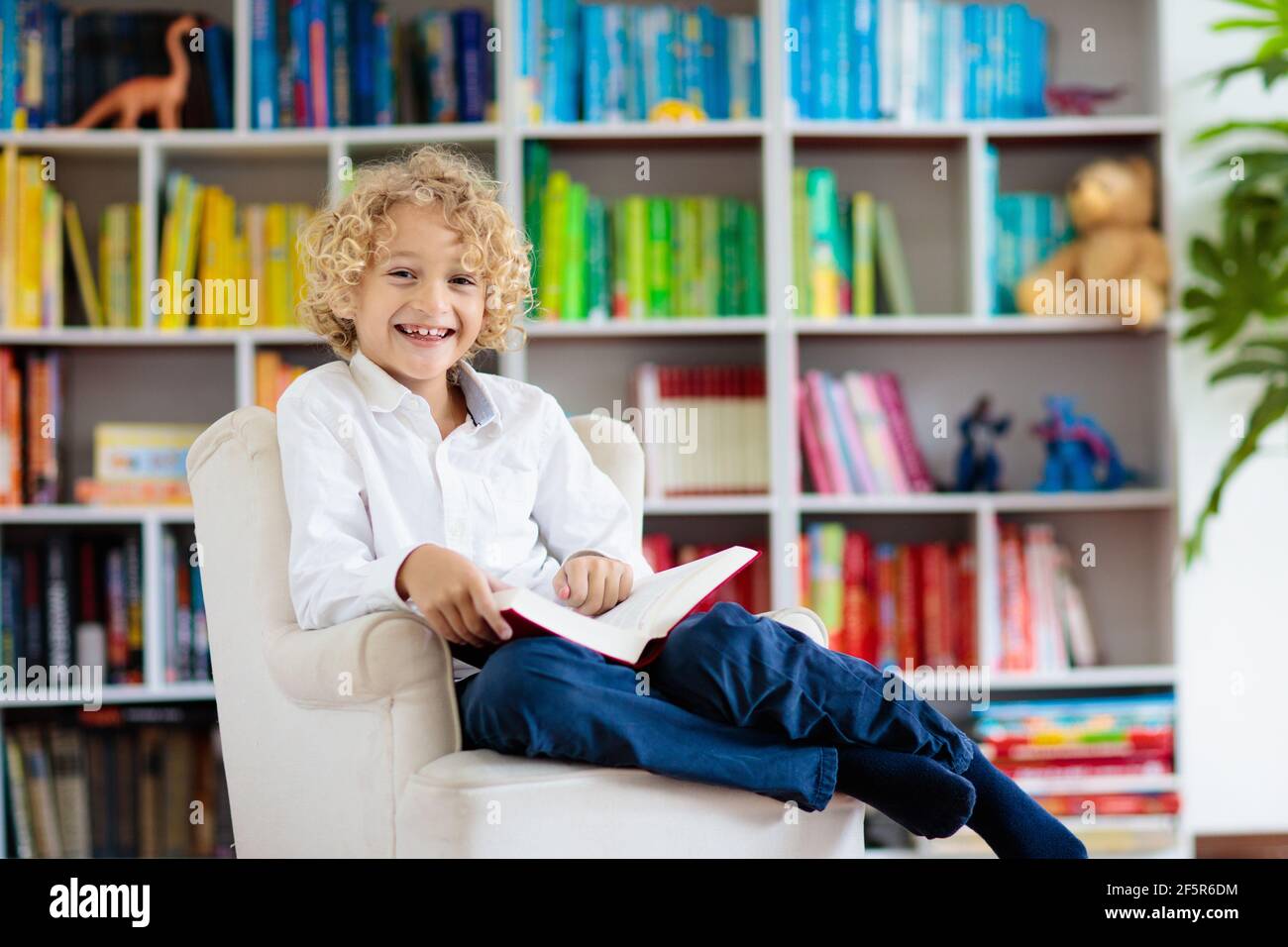 Child reading book. Kids read. Little boy at a colorful bookshelf doing ...