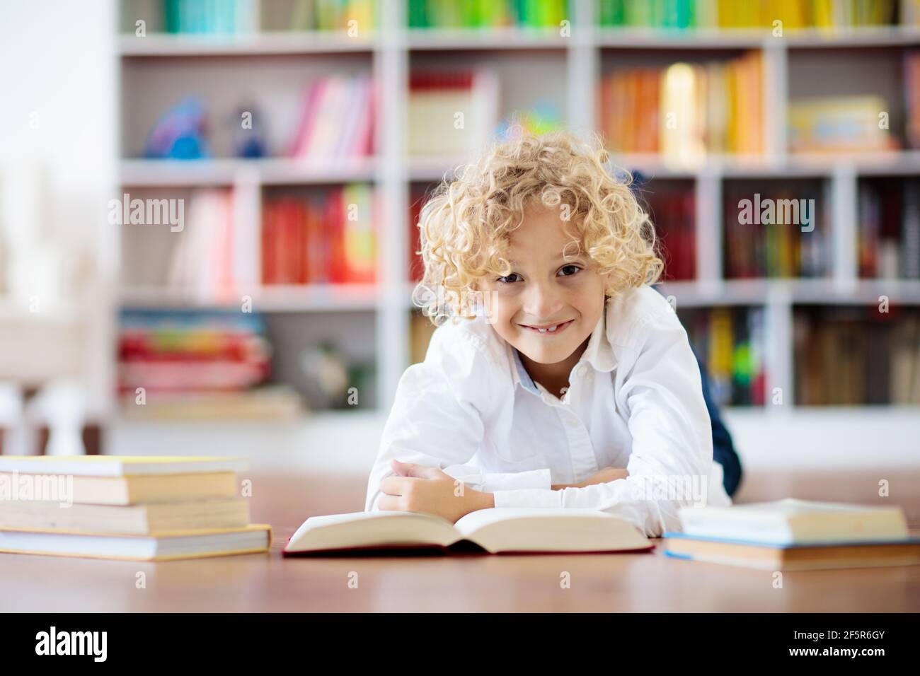 Child reading book. Kids read. Little boy at a colorful bookshelf doing ...