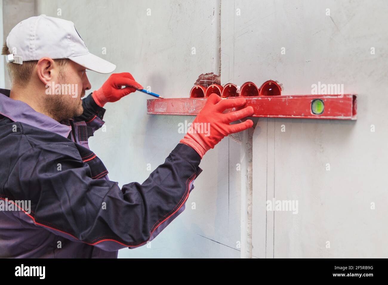 A man, an electrician marks out with a pencil, tape measure and a ...