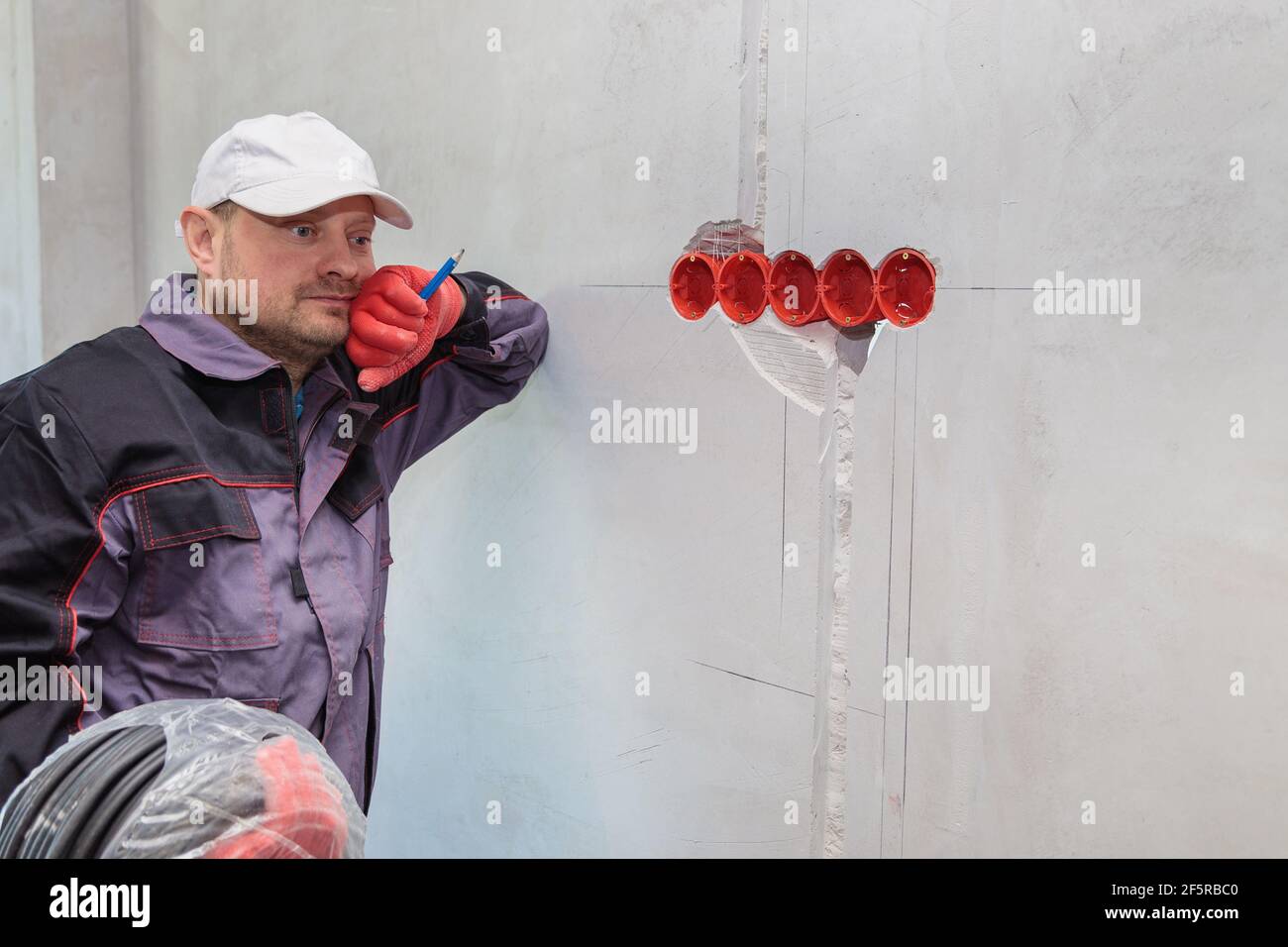 An electrician stands against the wall with an electrical cable for ...
