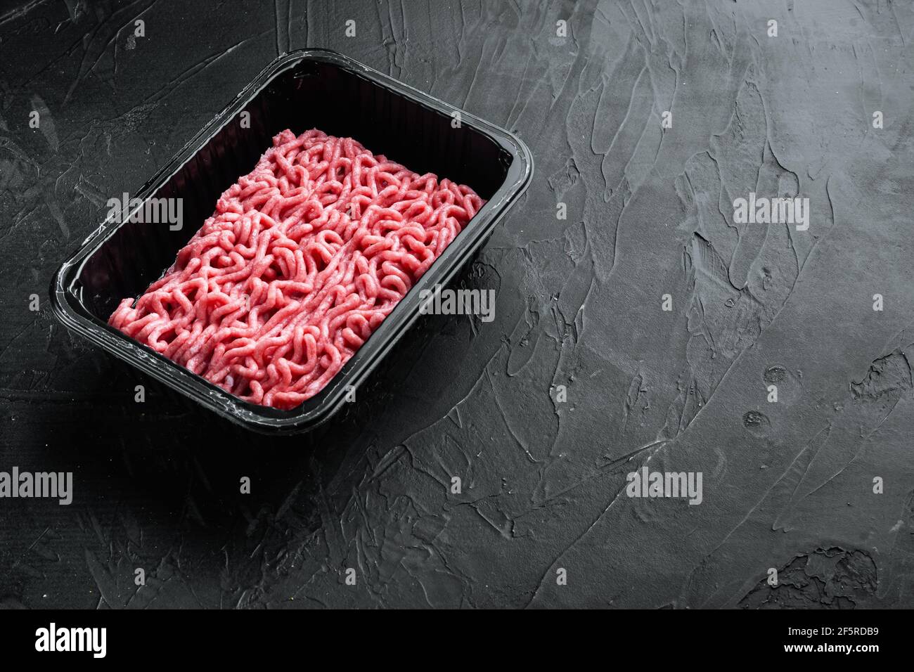 Ground beef meat in plastic tray set, on black stone background, with ...