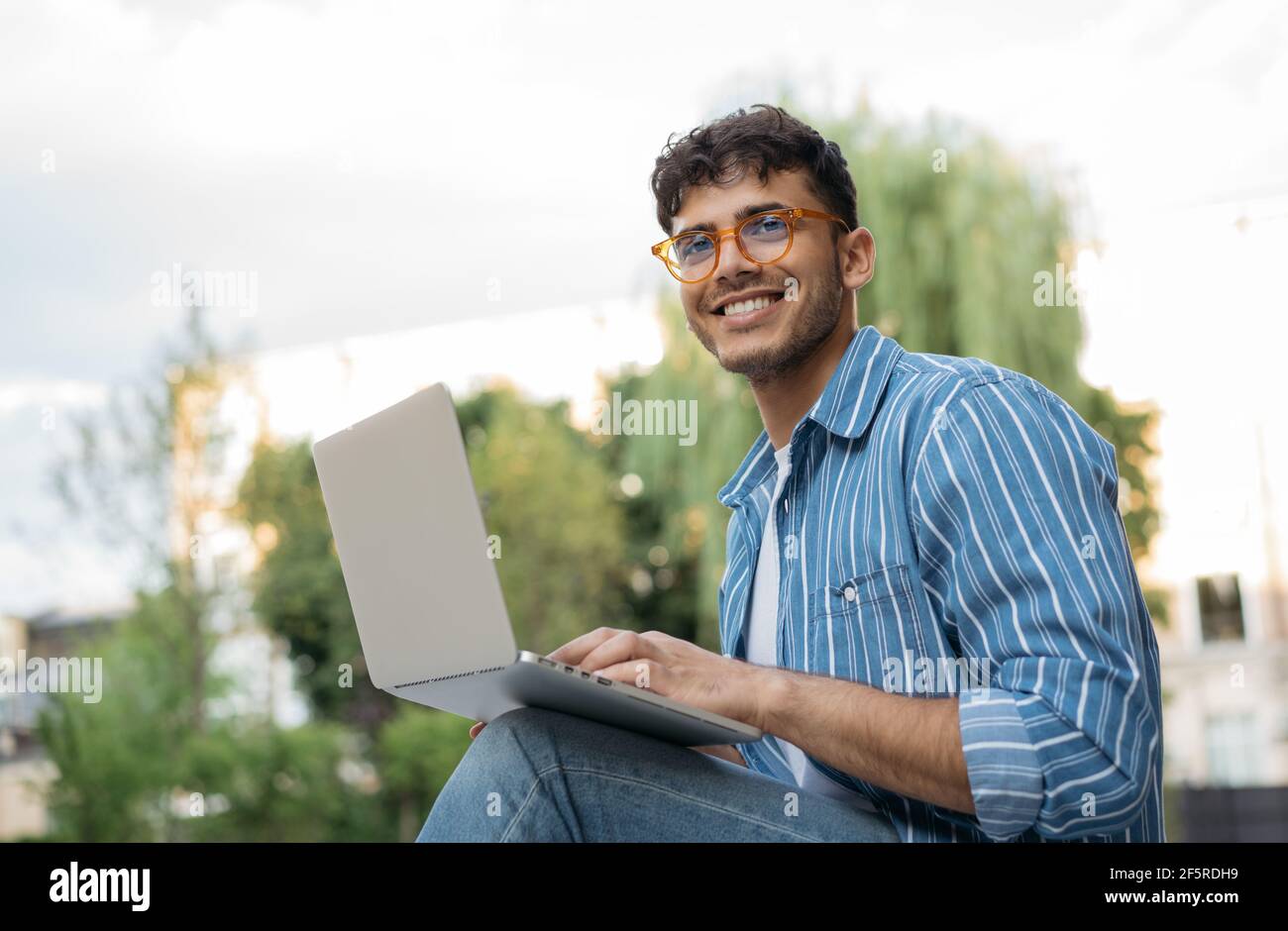 Portrait of handsome Indian copywriter using laptop computer, typing ...