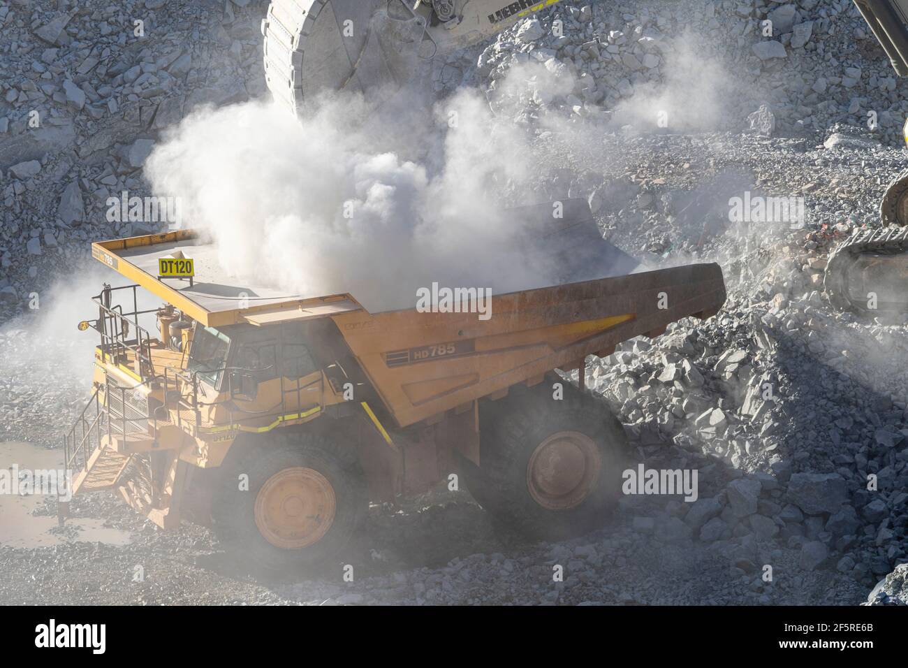 Dusty conditions as digger loads dump truck with ore at gold mine in ...