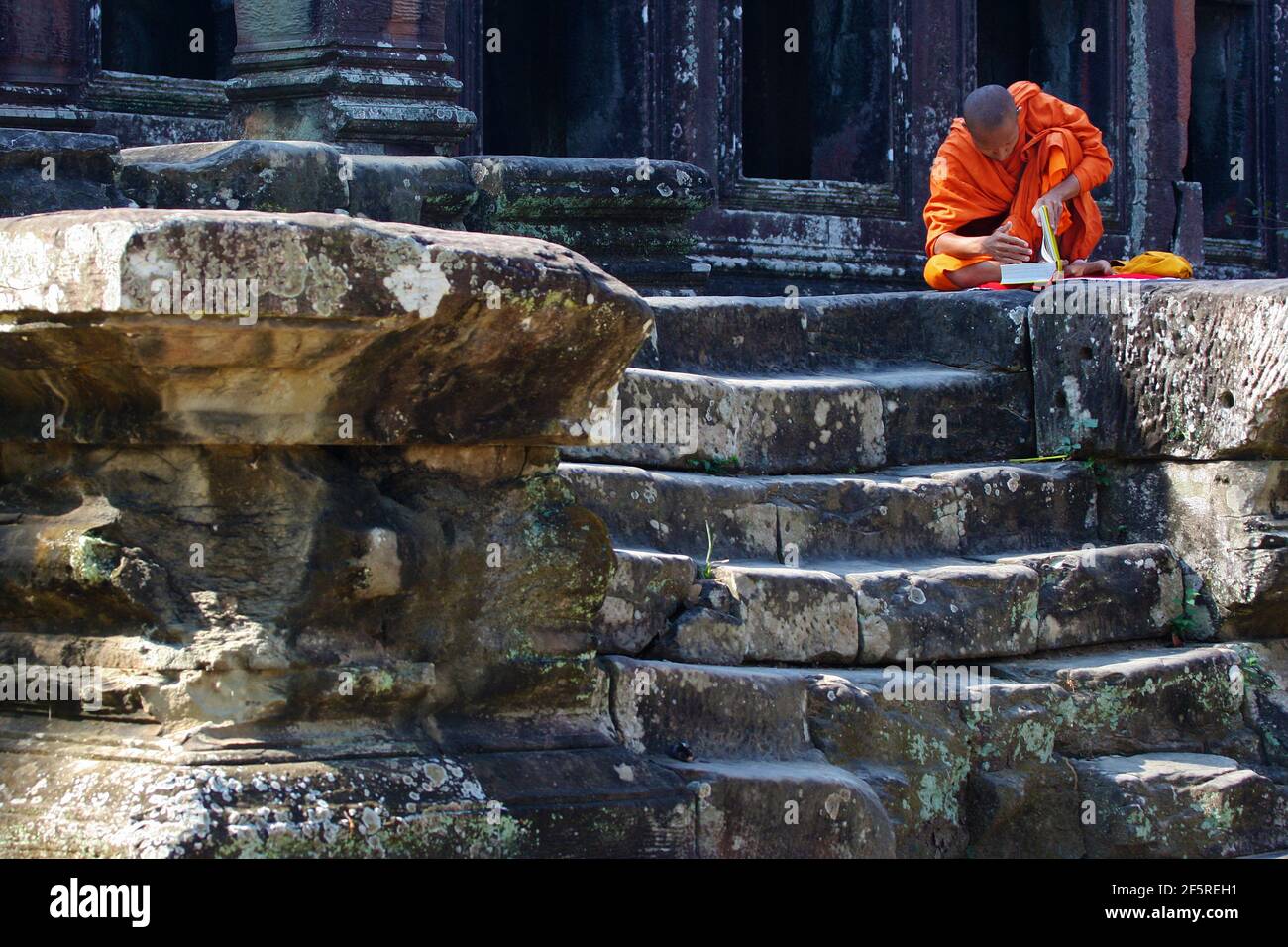Orange monk. A buddhist monk reads a holy book sitting out of an ...