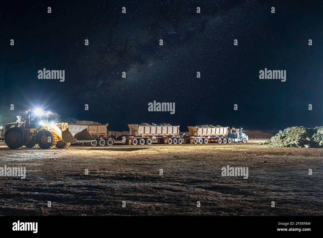 Open pit mining operation at night with drill rigs, dump trucks and ...