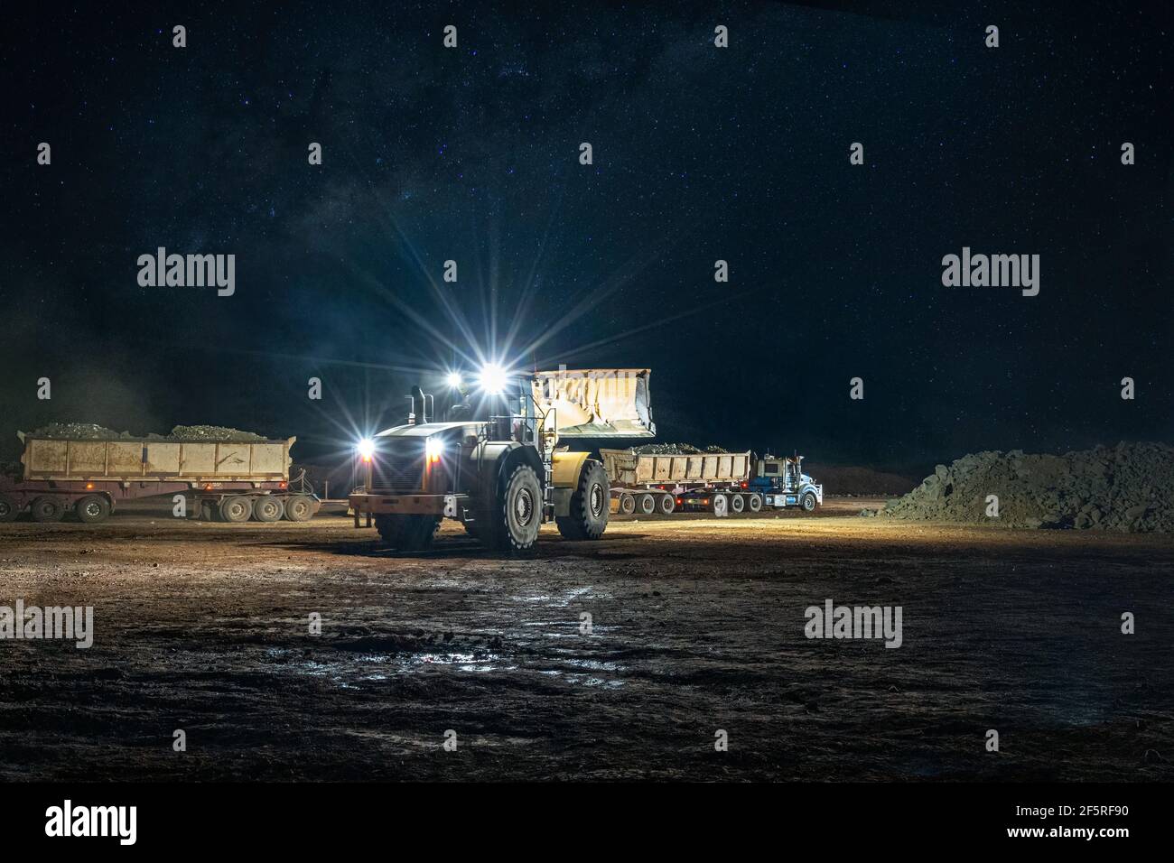 Open pit mining operation at night with drill rigs, dump trucks and ...