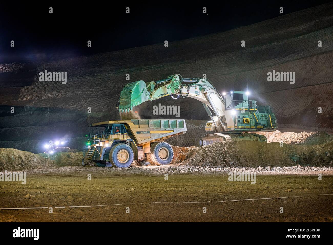 Open pit mining operation at night with drill rigs, dump trucks and ...