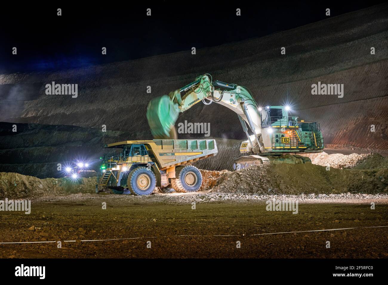 Open pit mining operation at night with drill rigs, dump trucks and ...