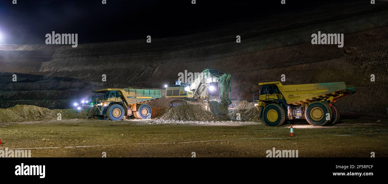 Open pit mining operation at night with drill rigs, dump trucks and ...
