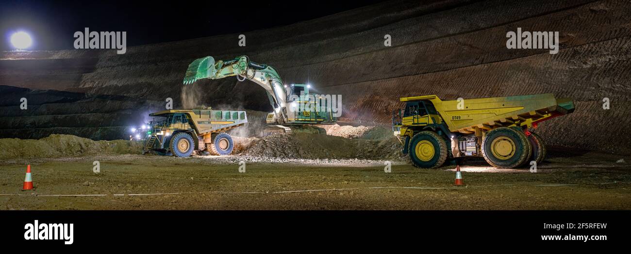 Open pit mining operation at night with drill rigs, dump trucks and ...