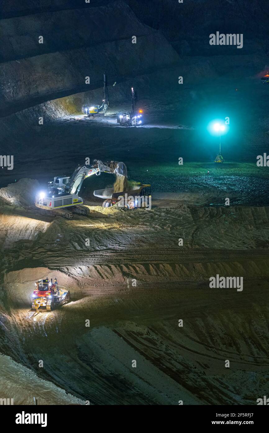 Open pit mining operation at night with drill rigs, dump trucks and ...