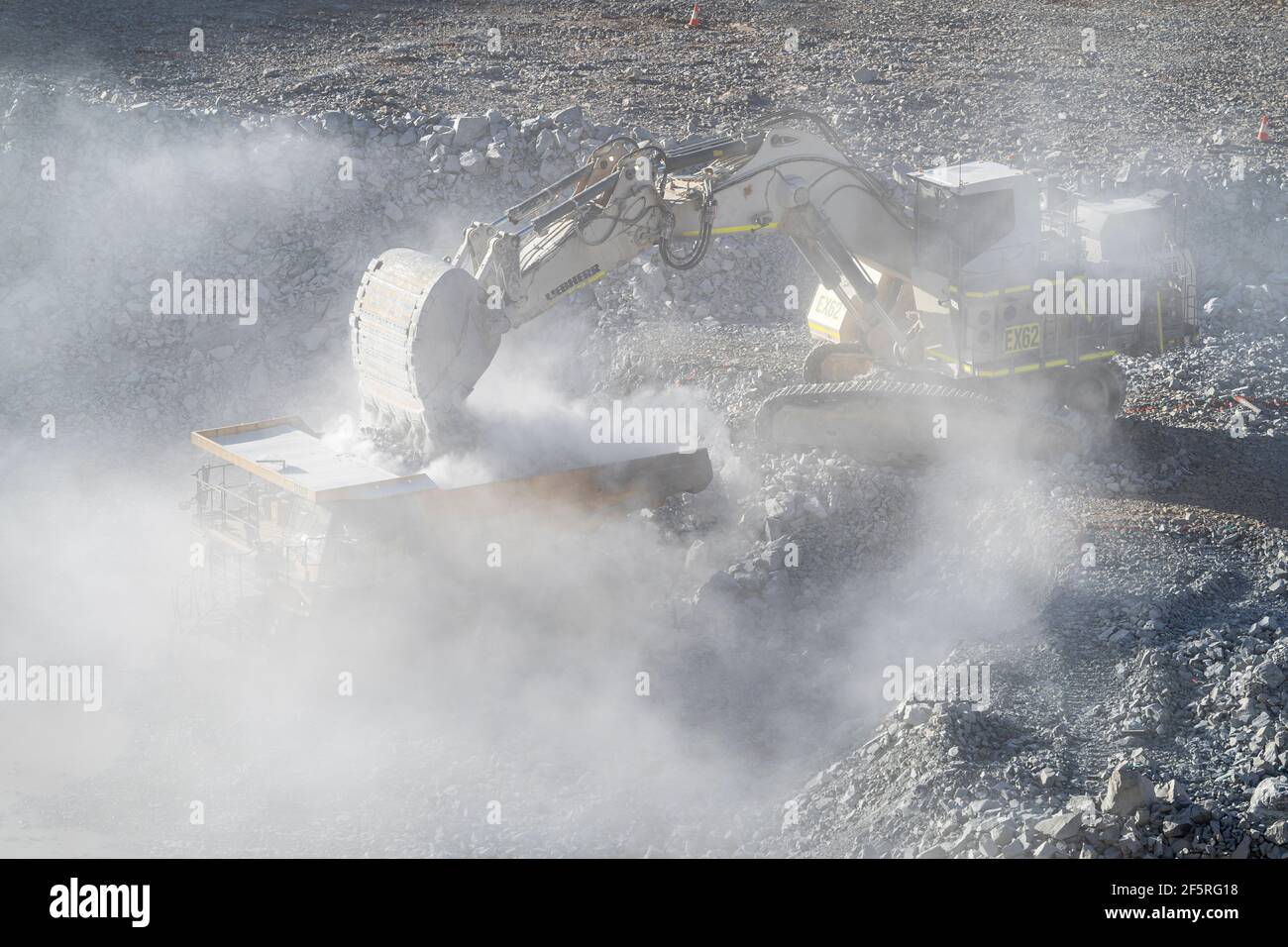 Dusty conditions as digger loads dump truck with ore at gold mine in ...