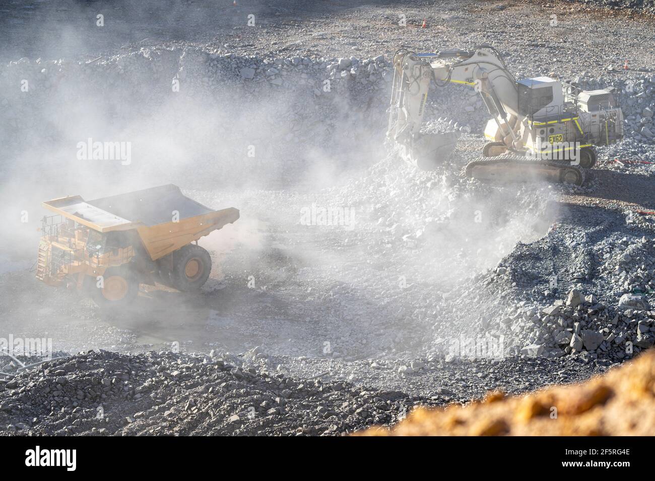 Dusty conditions as digger loads dump truck with ore at gold mine in ...