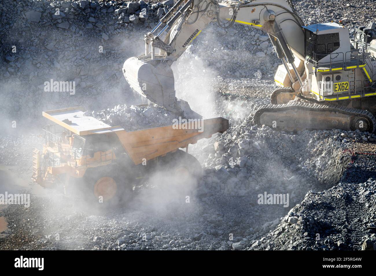 Dusty conditions as digger loads dump truck with ore at gold mine in ...