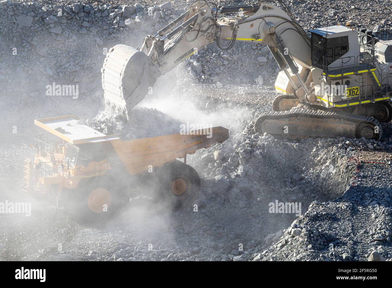 Dusty conditions as digger loads dump truck with ore at gold mine in ...
