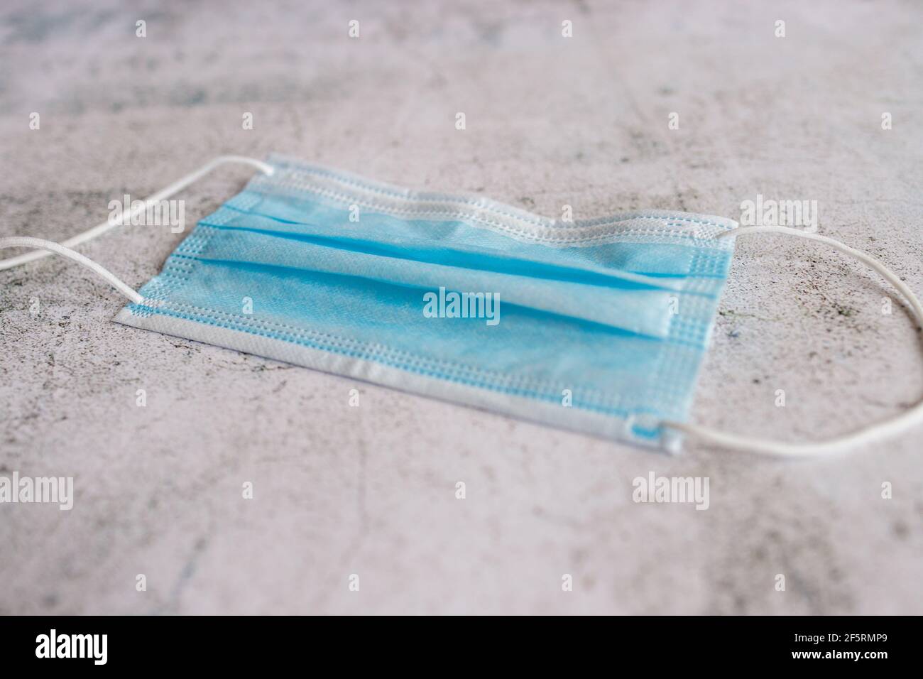 Used surgical face mask isolated on concrete floor. Improperly ...