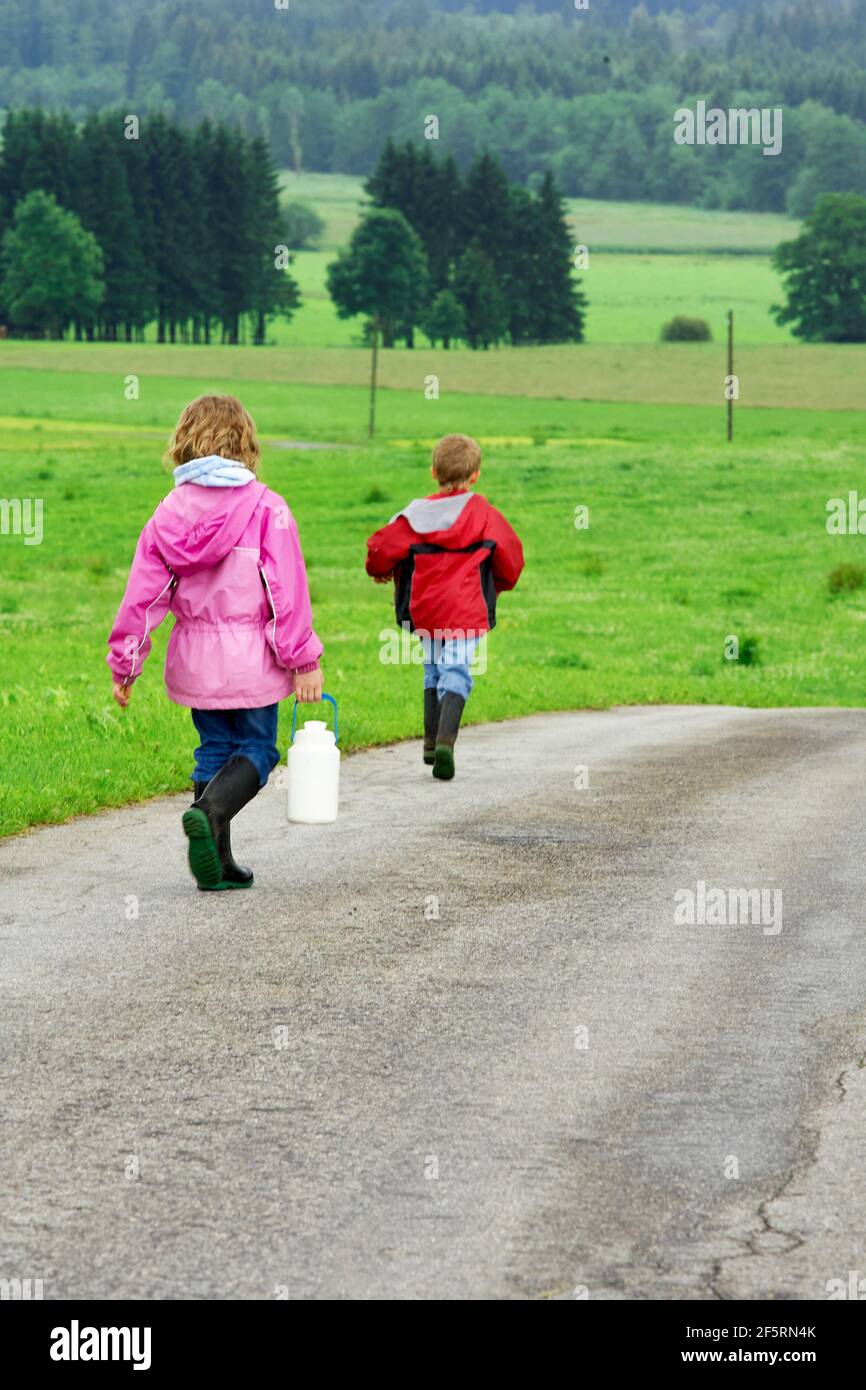 Back view of unrecognizable kids with milk can walking on asphalt road ...