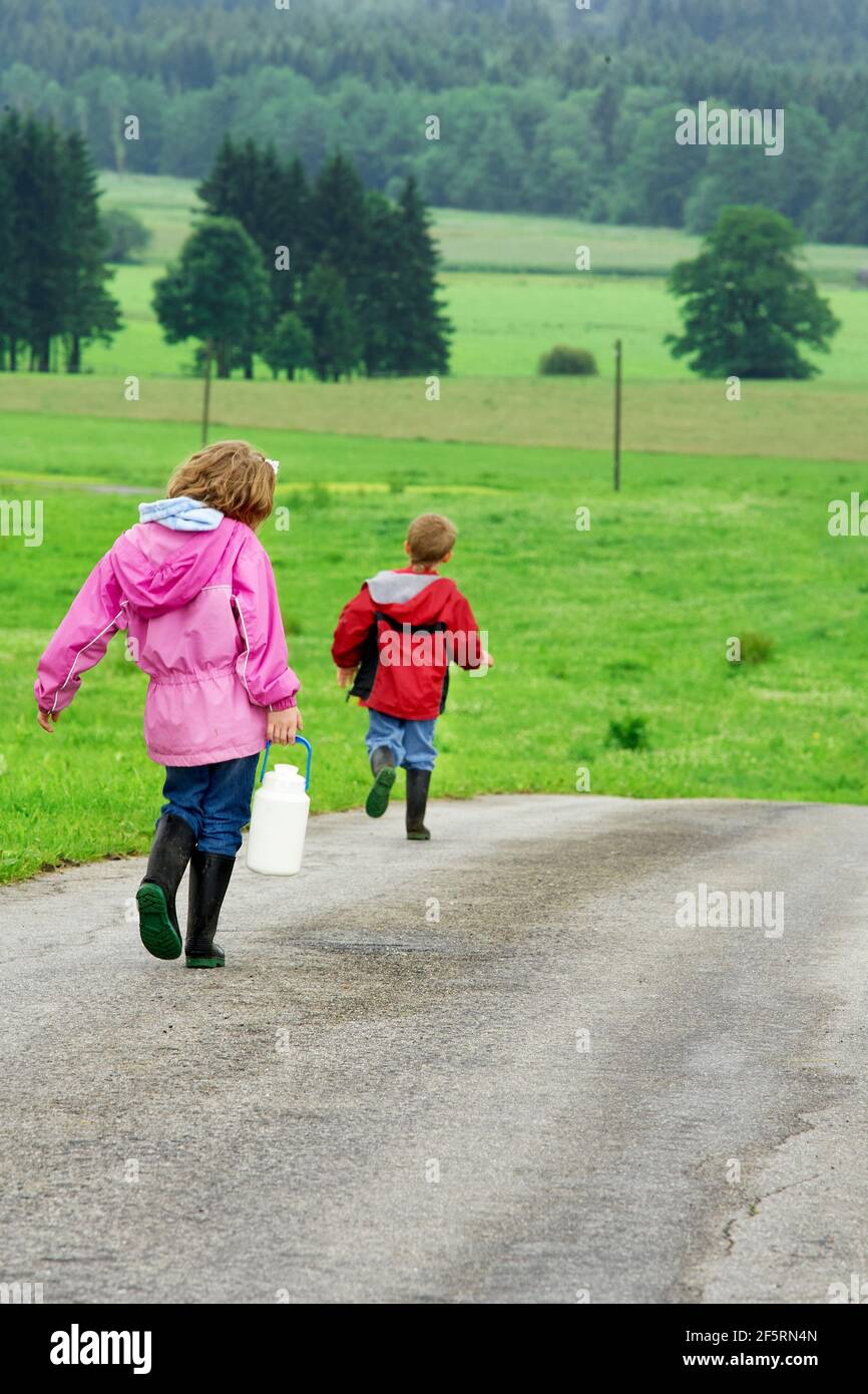 Back view of unrecognizable kids with milk can walking on asphalt road ...
