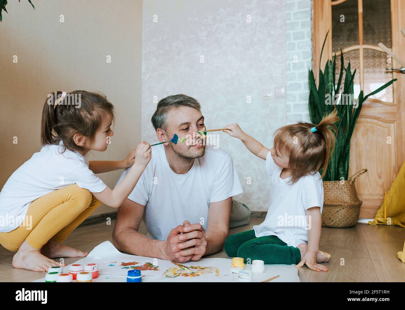 two little girls paint on dad's face with paint Stock Photo - Alamy