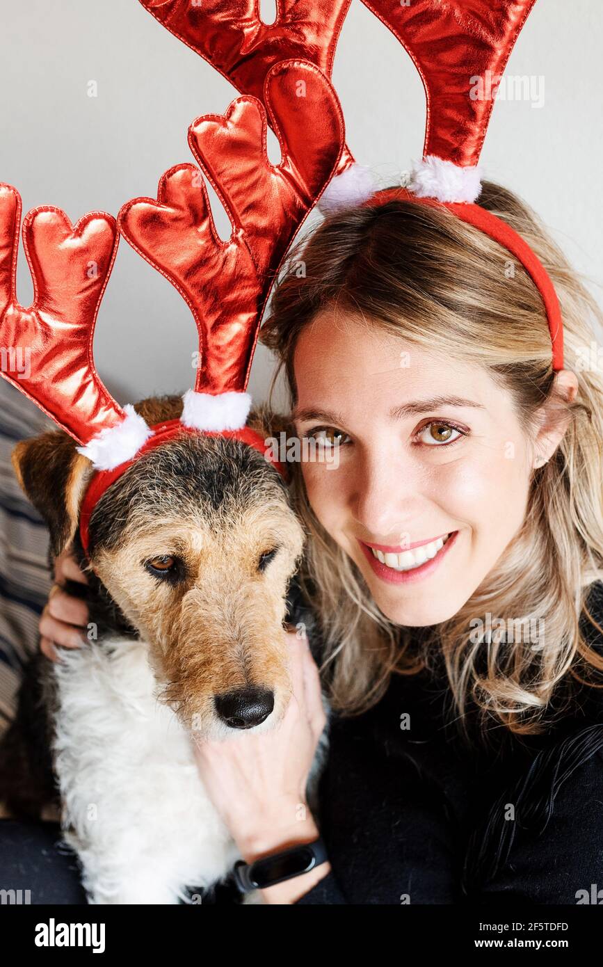 Happy female in decorative deer horns cuddling adorable purebred dog ...