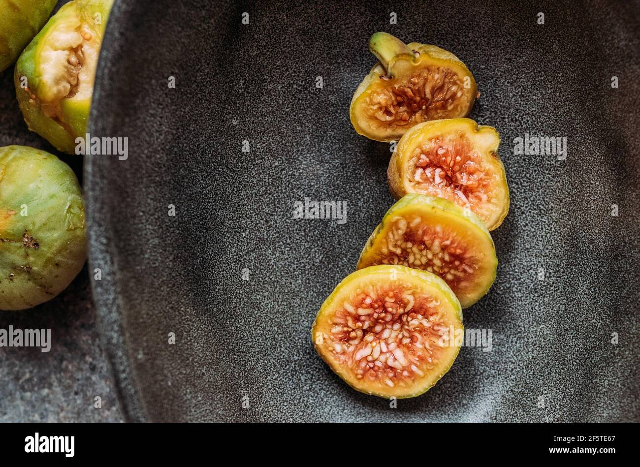 Green fig slices in modern black bowl on the table with grunge texture ...