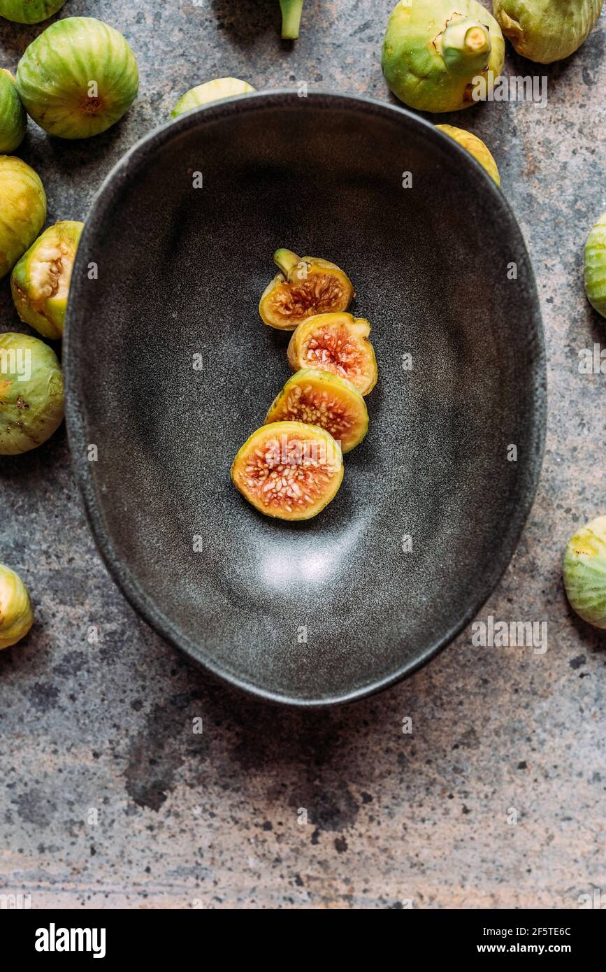 Green fig slices in modern black bowl on the table with grunge texture ...