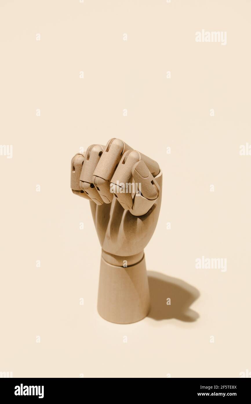 High angle of wooden hand showing clenched fist on beige background in ...