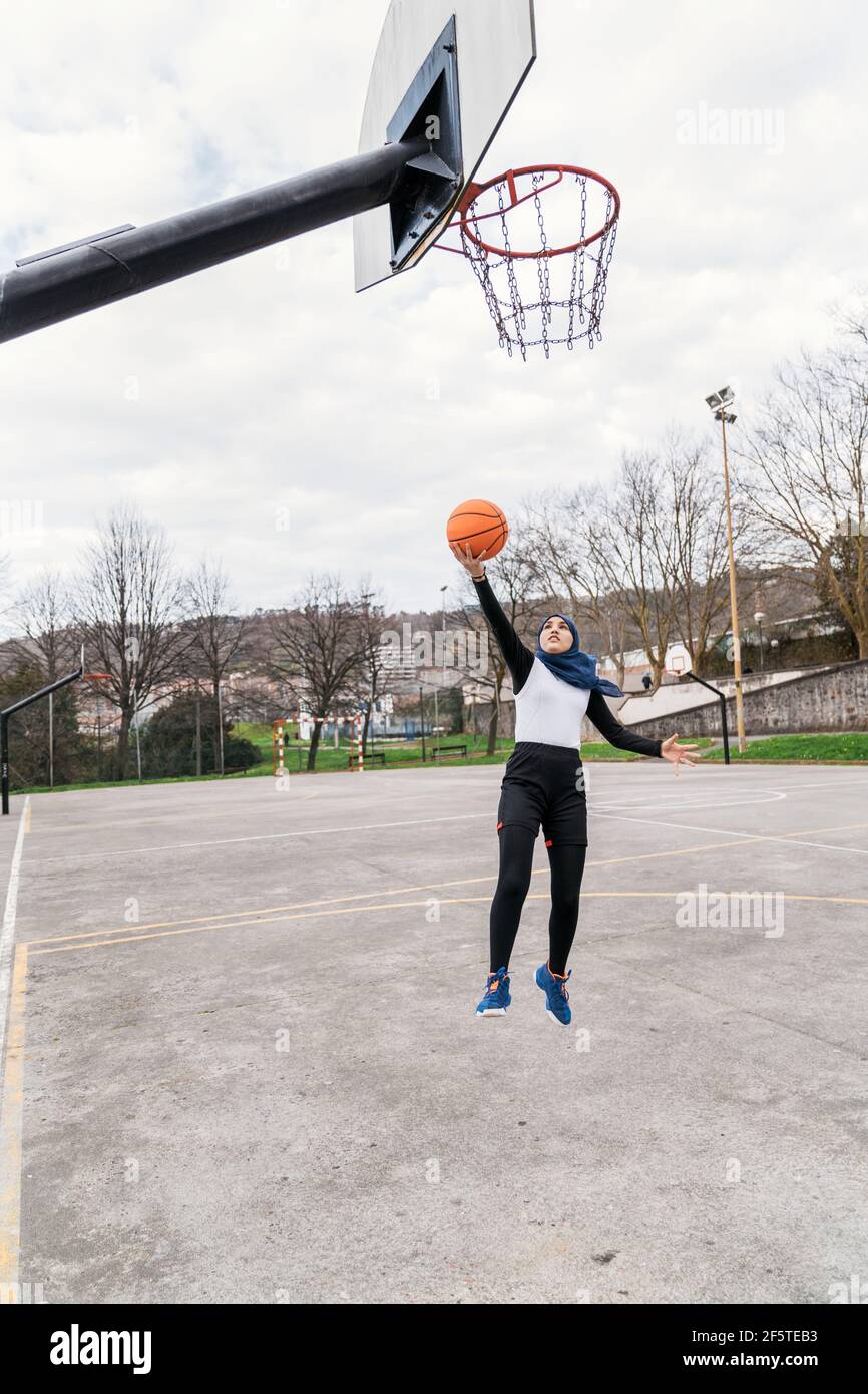 Muslim female streetball player jumping above ground and scoring ball ...