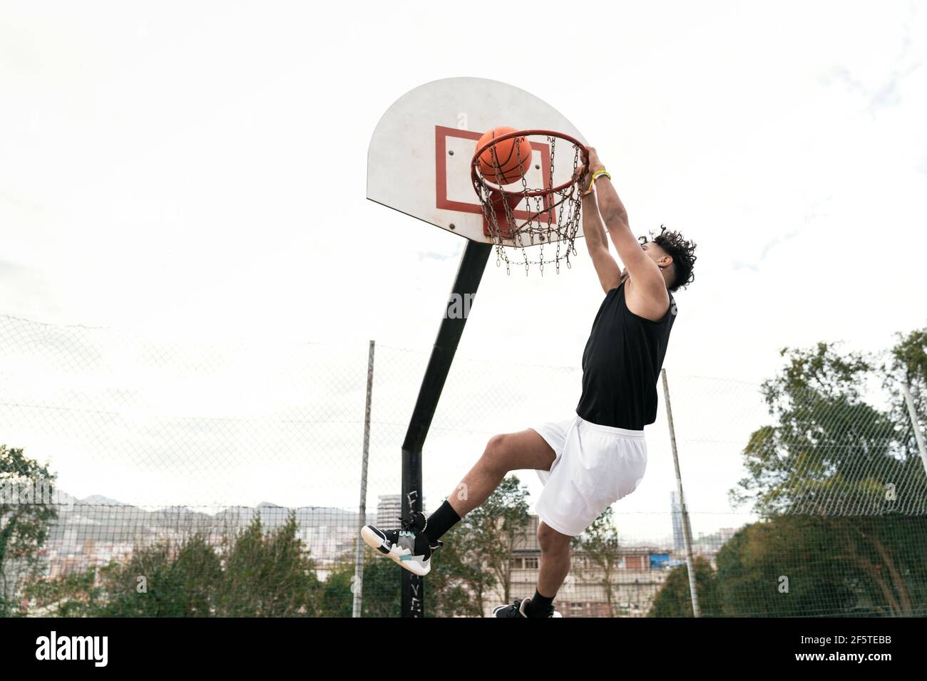 Side view of ethnic male streetball player performing slam dunk in ...