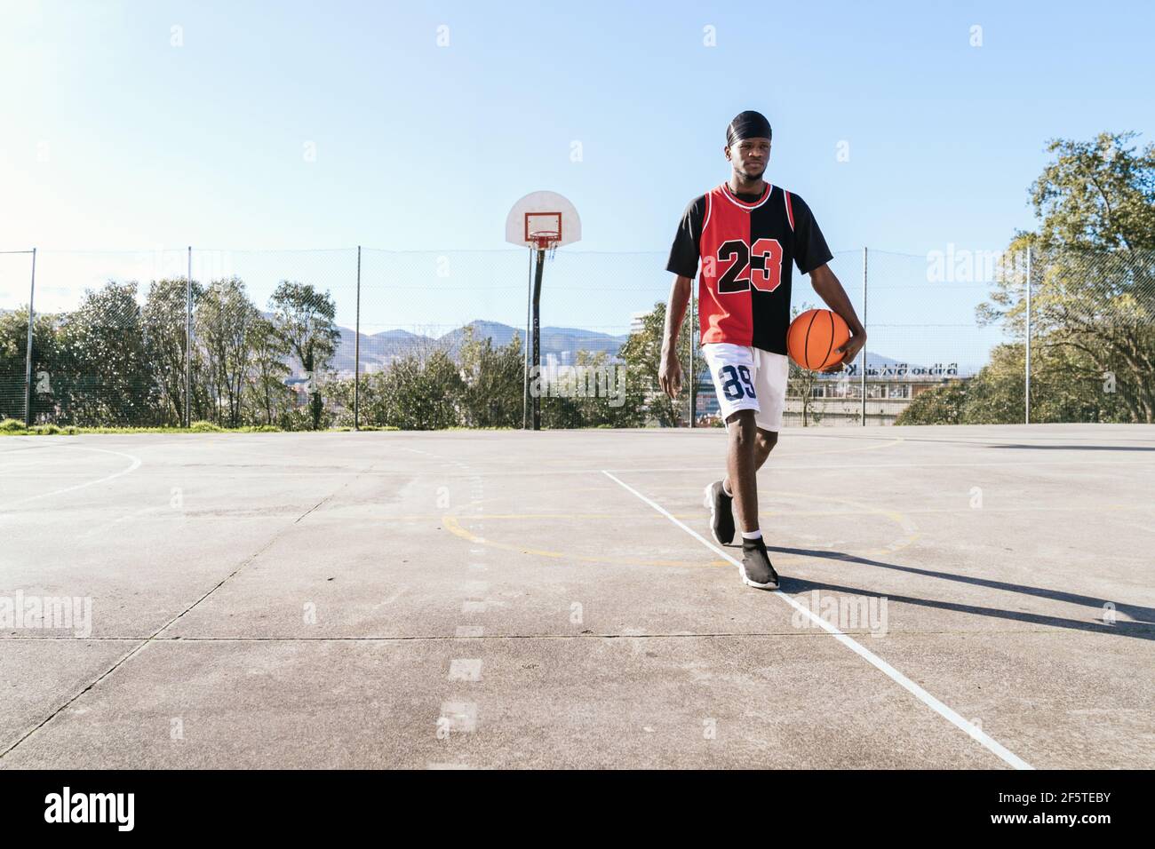 Serious African American male streetball player in uniform walking with ...