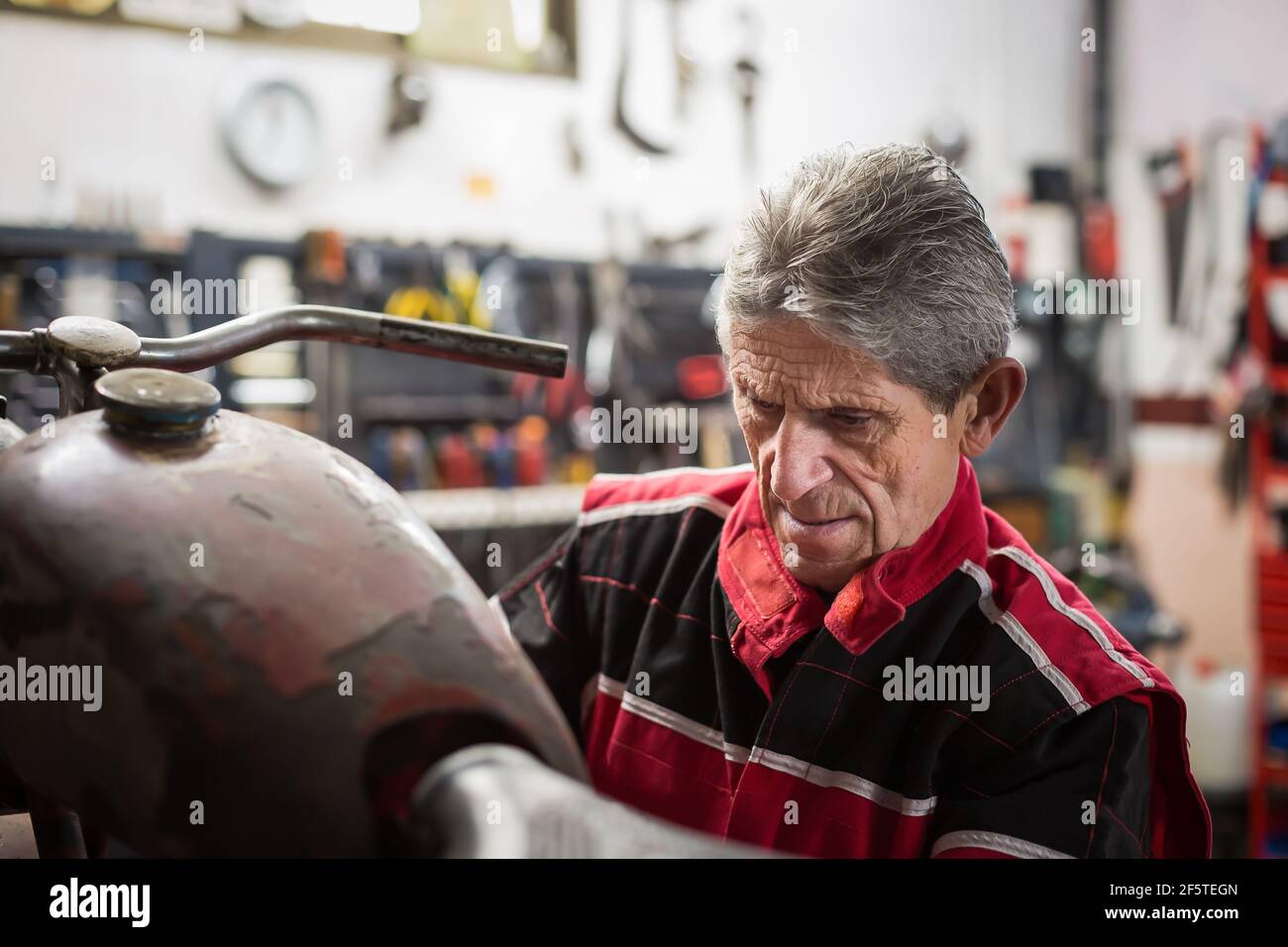Senior male mechanic repairing old rusty disassembled motorbike while ...