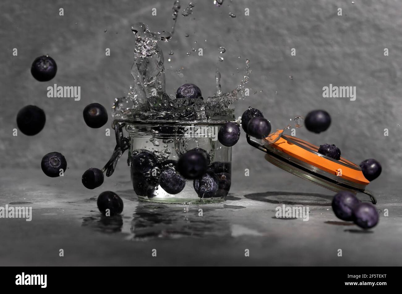Fresh blueberries falling in glass jar and splashing water on gray ...
