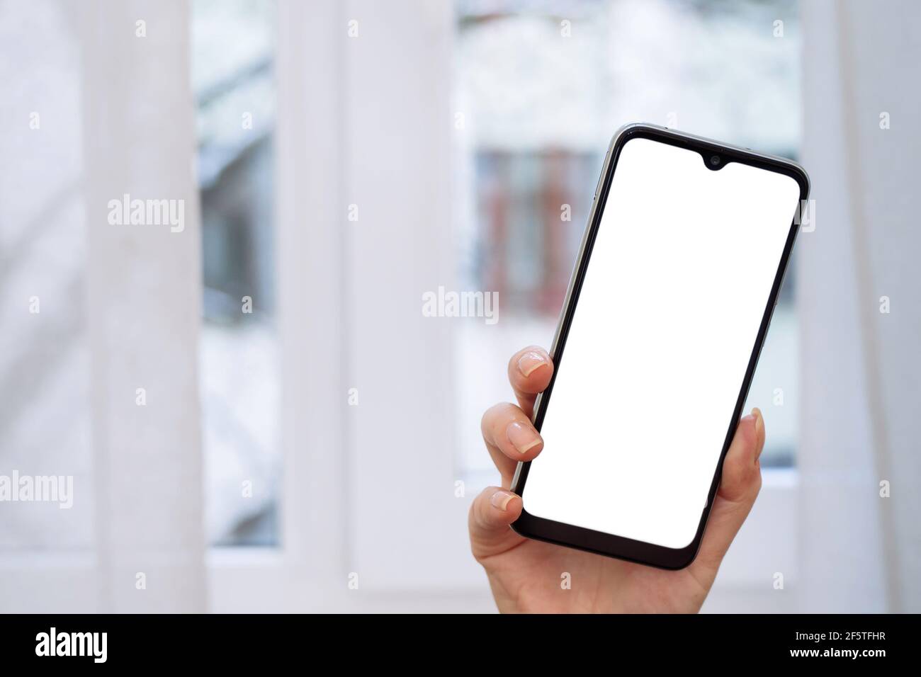 Female hand holding mobile phone with blank white screen over bright ...