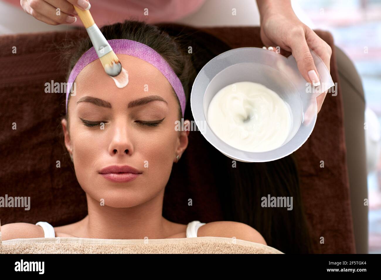 Cosmetician applying facial cream mask on woman face with closed eyes ...