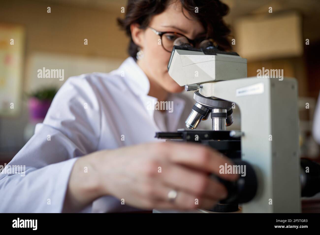 A young female scientist looking through the microscope in a working ...