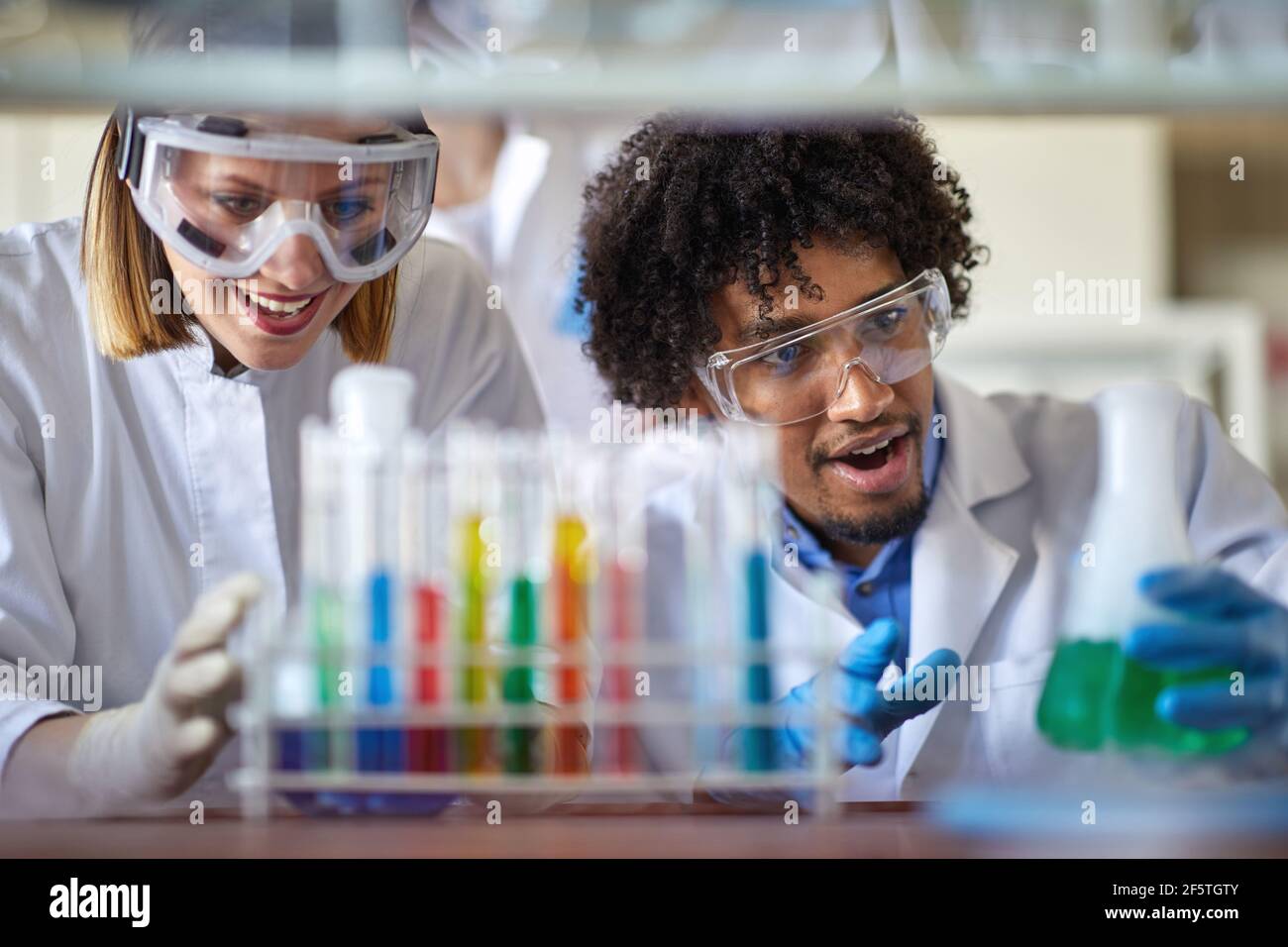Young colleagues in a protective gear observe chemical reactions in a ...