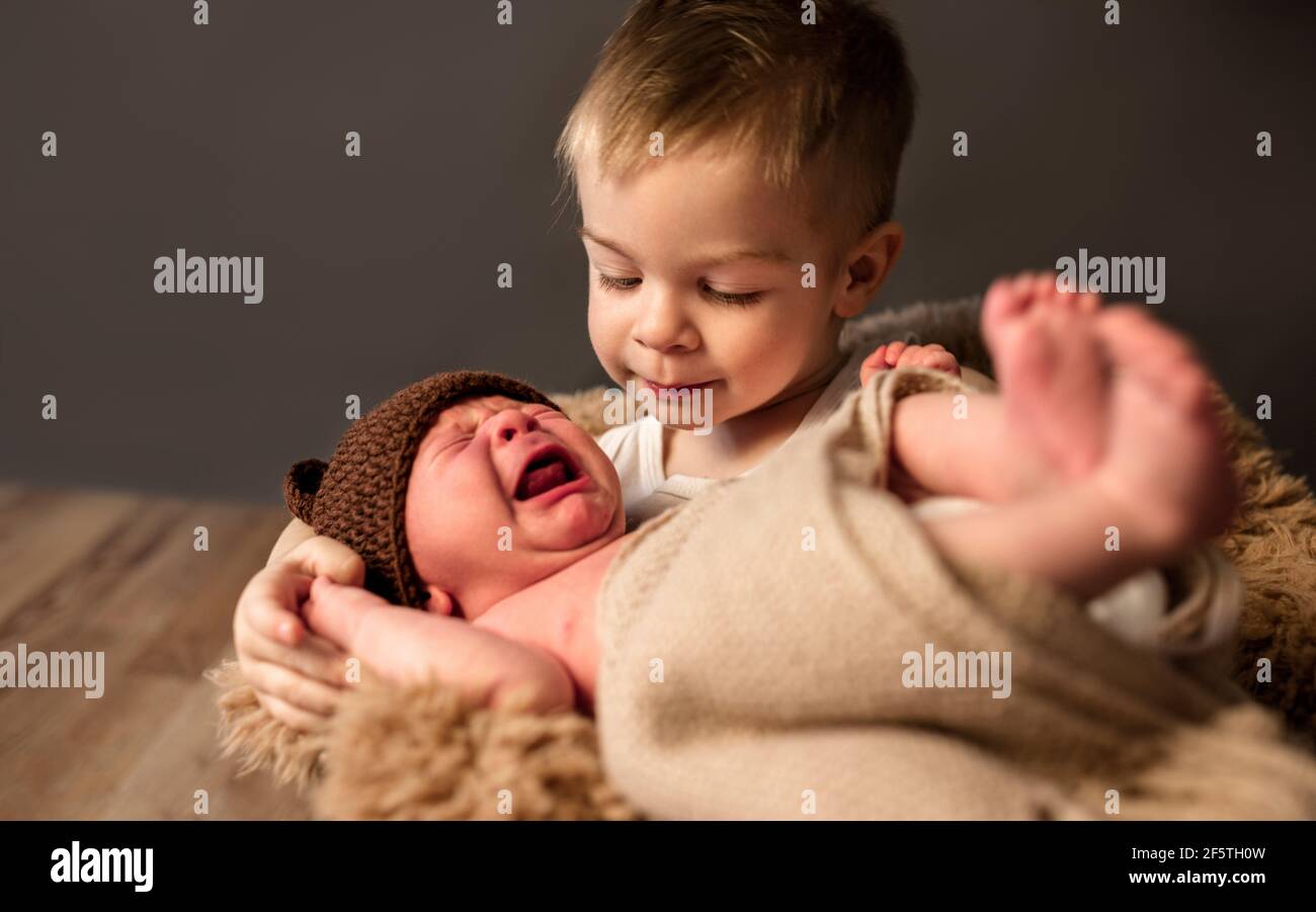 Little boy holding his newborn brother crying Stock Photo - Alamy