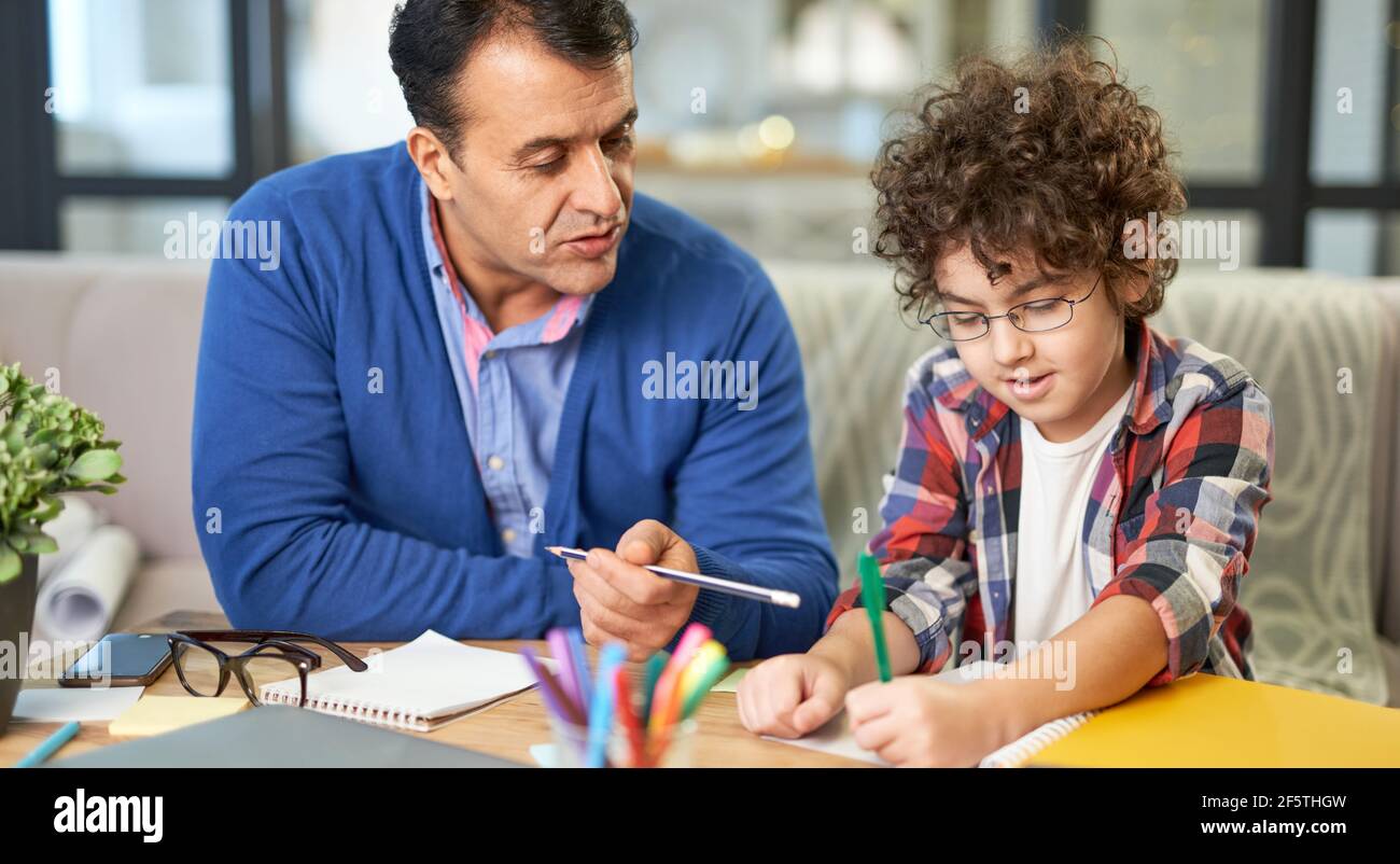 Caring teacher. Middle aged latin father checking homework, helping his ...