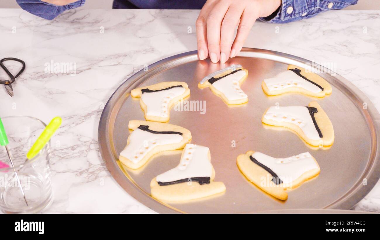 Decorating ice skate shaped sugar cookies with black color royal icing ...