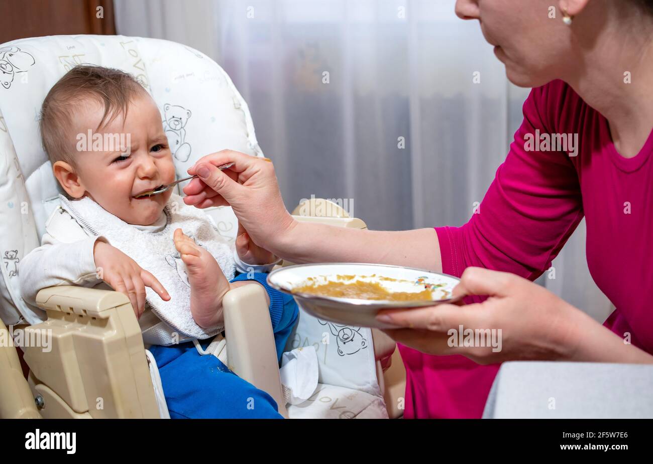 Baby boy sitting in a feeding chair, eating his first food from the ...