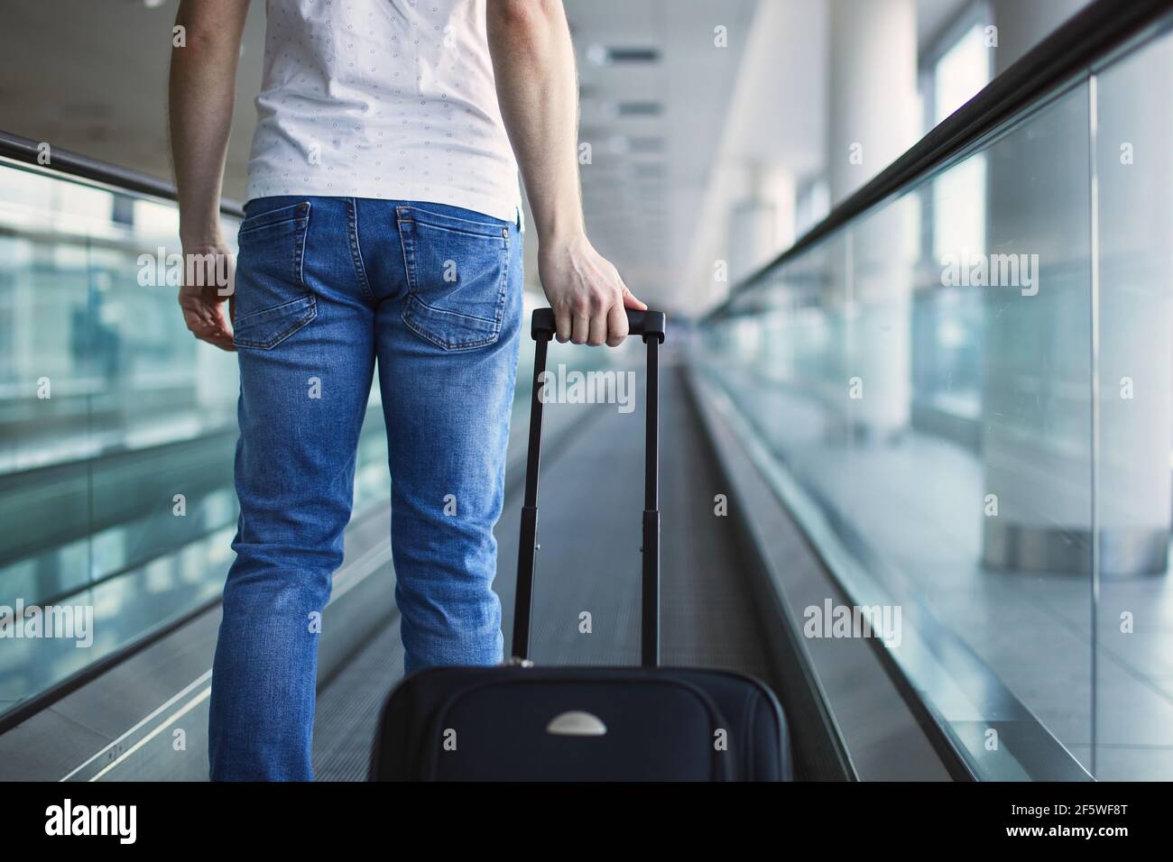Man walking with suitcase. Rear view of traveler on moving walkway at ...