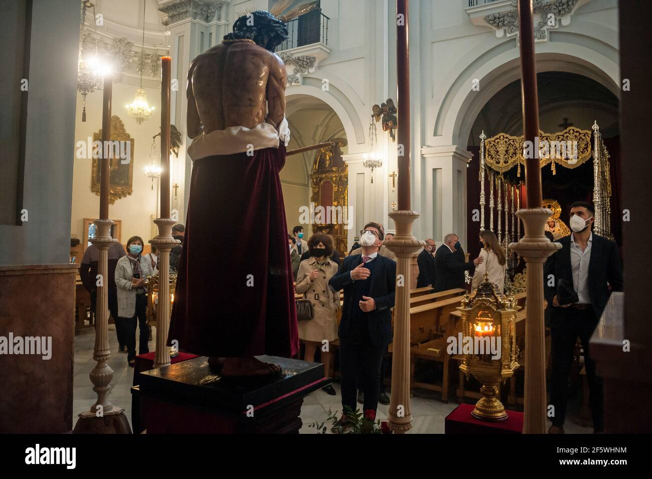 A believer wearing a face mask is seen praying in front of a figure of ...