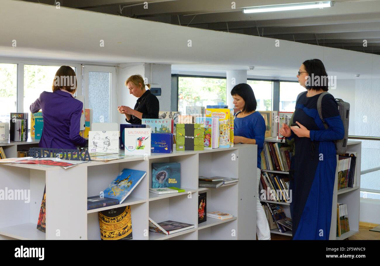 People visitors standing in front of shelf with books and reading books ...
