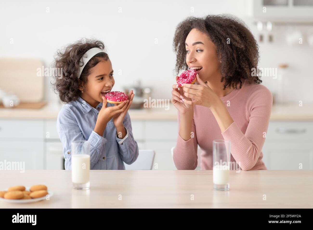 Black mother and daughter eating sweet food in kitchen Stock Photo - Alamy