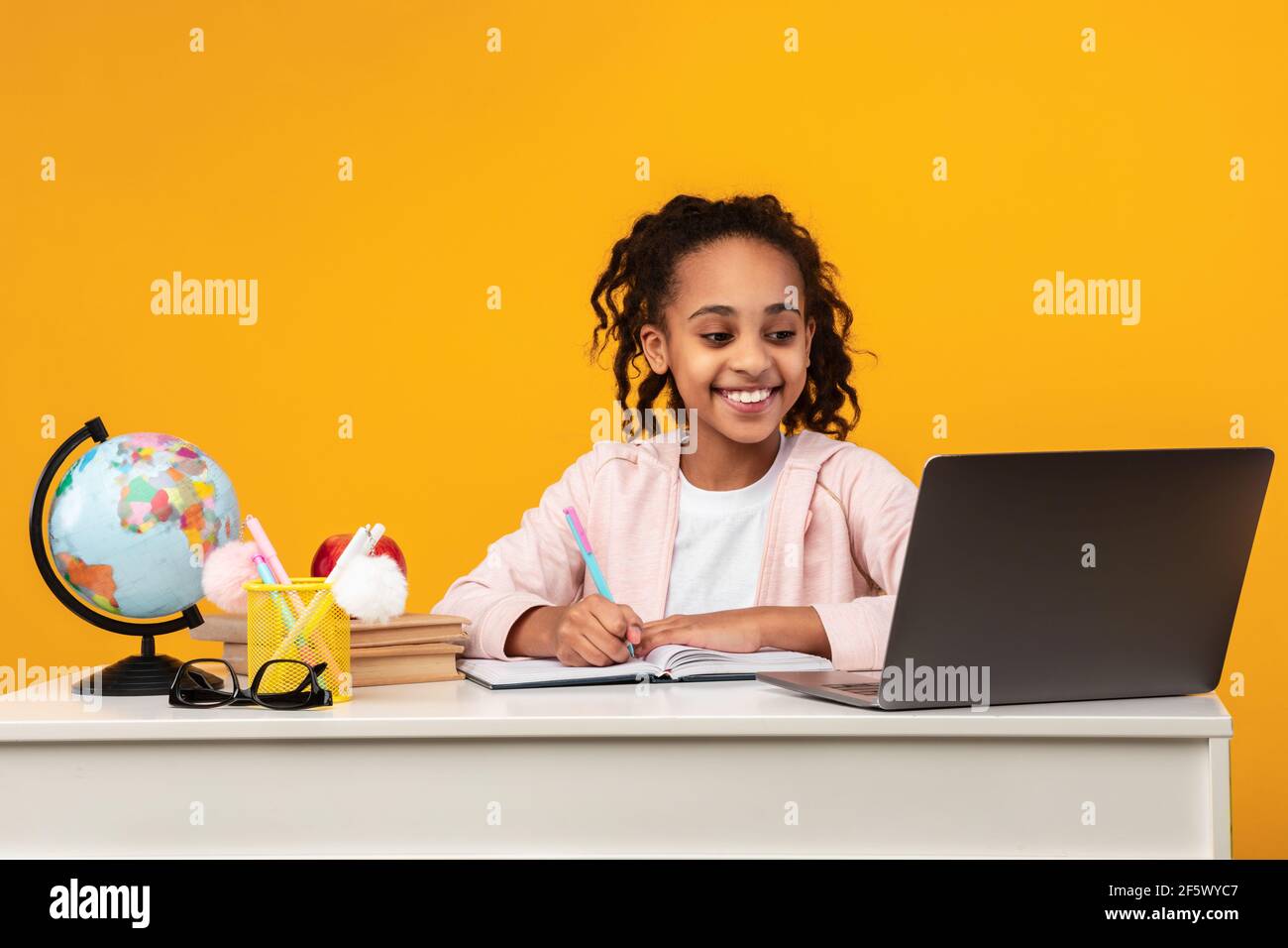 Portrait of smiling black girl sitting at table and writing Stock Photo ...