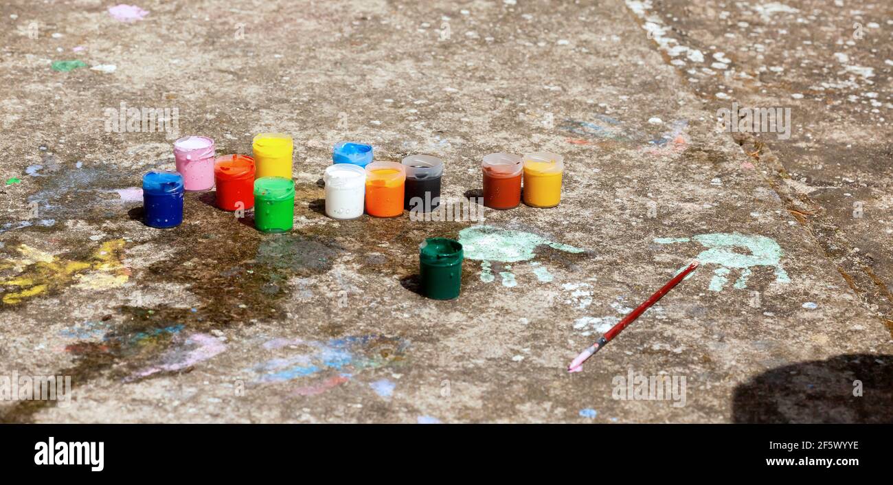 Colorful small paint containers and child's hands printed on the ground ...