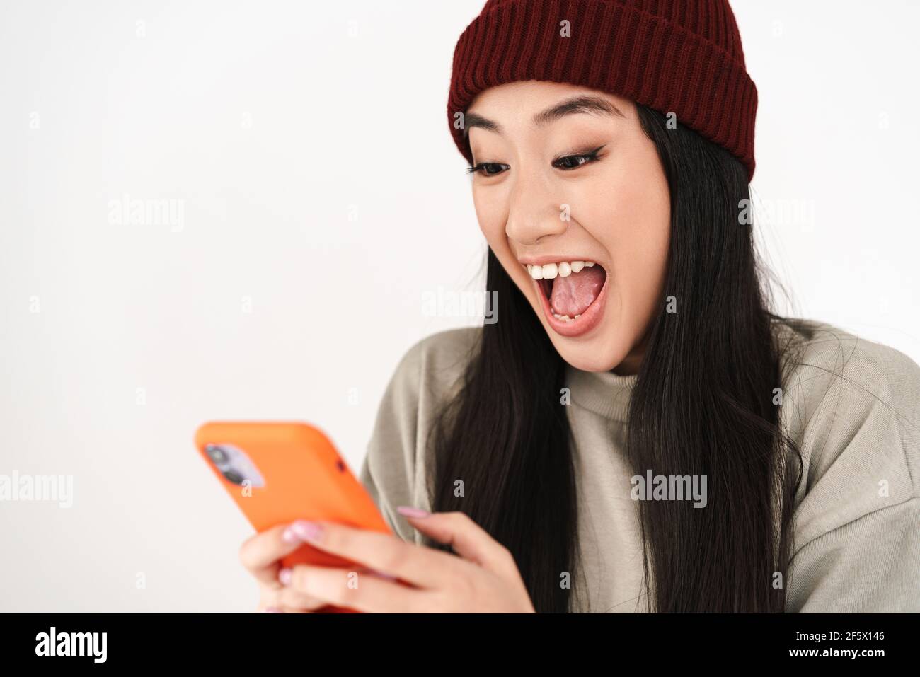 Asian excited nice girl exclaiming while using mobile phone isolated ...