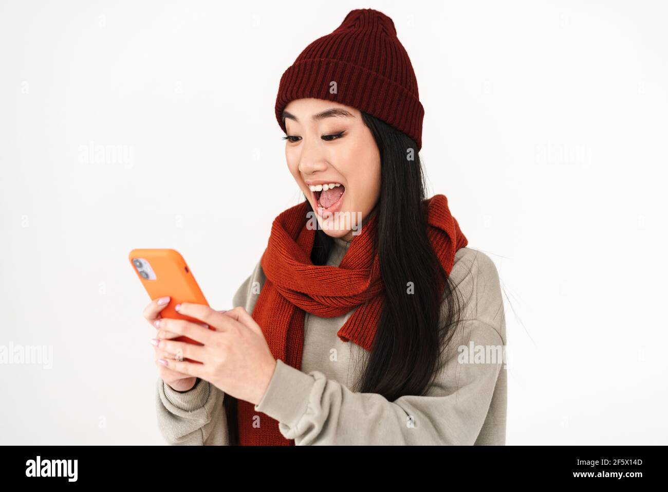 Asian excited nice girl exclaiming while using mobile phone isolated ...