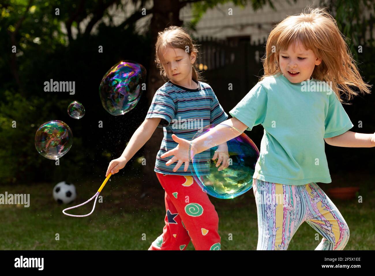 Two happy little girls, children playing with large soap bubbles ...
