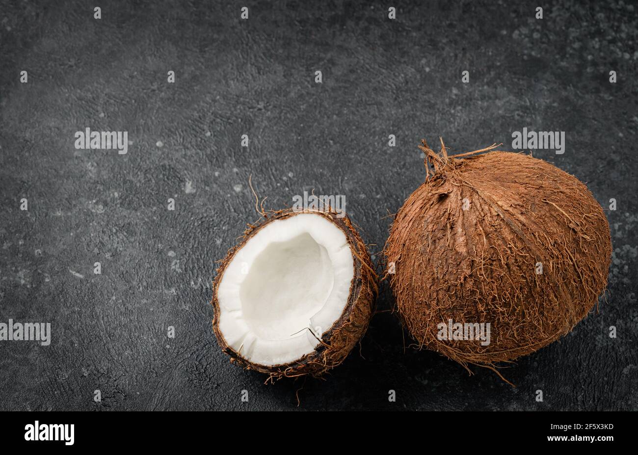 Whole and a half of cracked coconut on dark concrete background. Copy ...